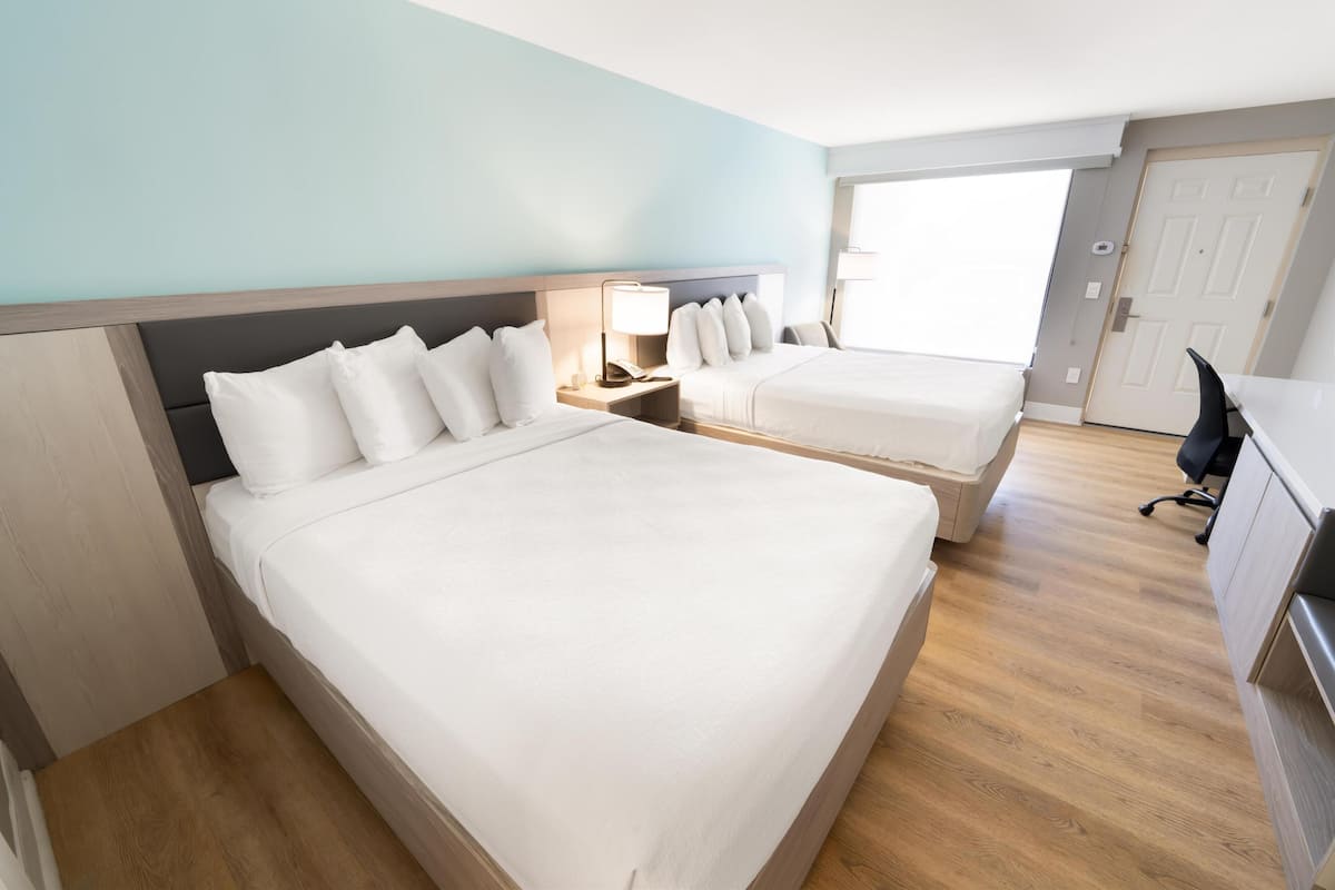 Quarto de hotel com duas camas, uma escrivaninha e uma cadeira.