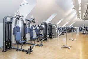 Academia com várias máquinas Nautilus, piso de madeira e teto alto com claraboias.