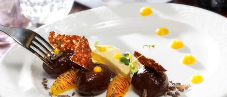 Um prato branco com uma sobremesa composta por esferas de chocolate, um pedaço retangular de bolo e guarnições.