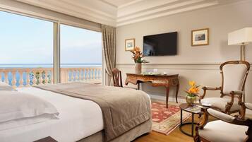 Quarto de hotel com uma cama grande, uma escrivaninha com cadeira, televisão e vista para o mar.
