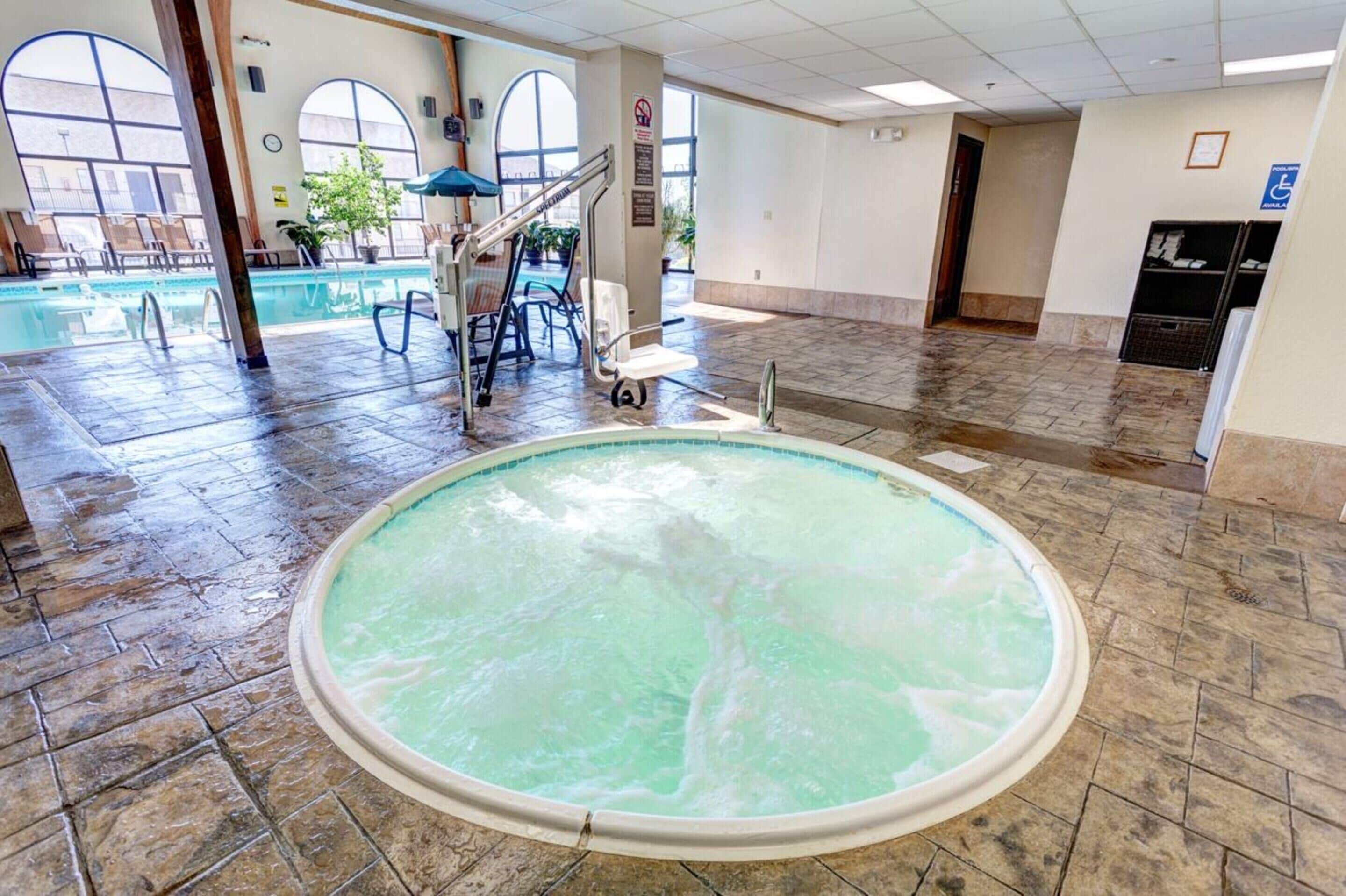 Piscina interior com chão ladrilhado, cadeira de salva-vidas e rampa de acesso para cadeiras de rodas.