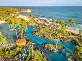 Um resort com piscina, palmeiras e uma praia.