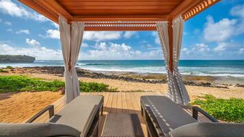 Um espaço de relaxamento à beira-mar, com mobiliário de vime e um deck de madeira com vista para o oceano.