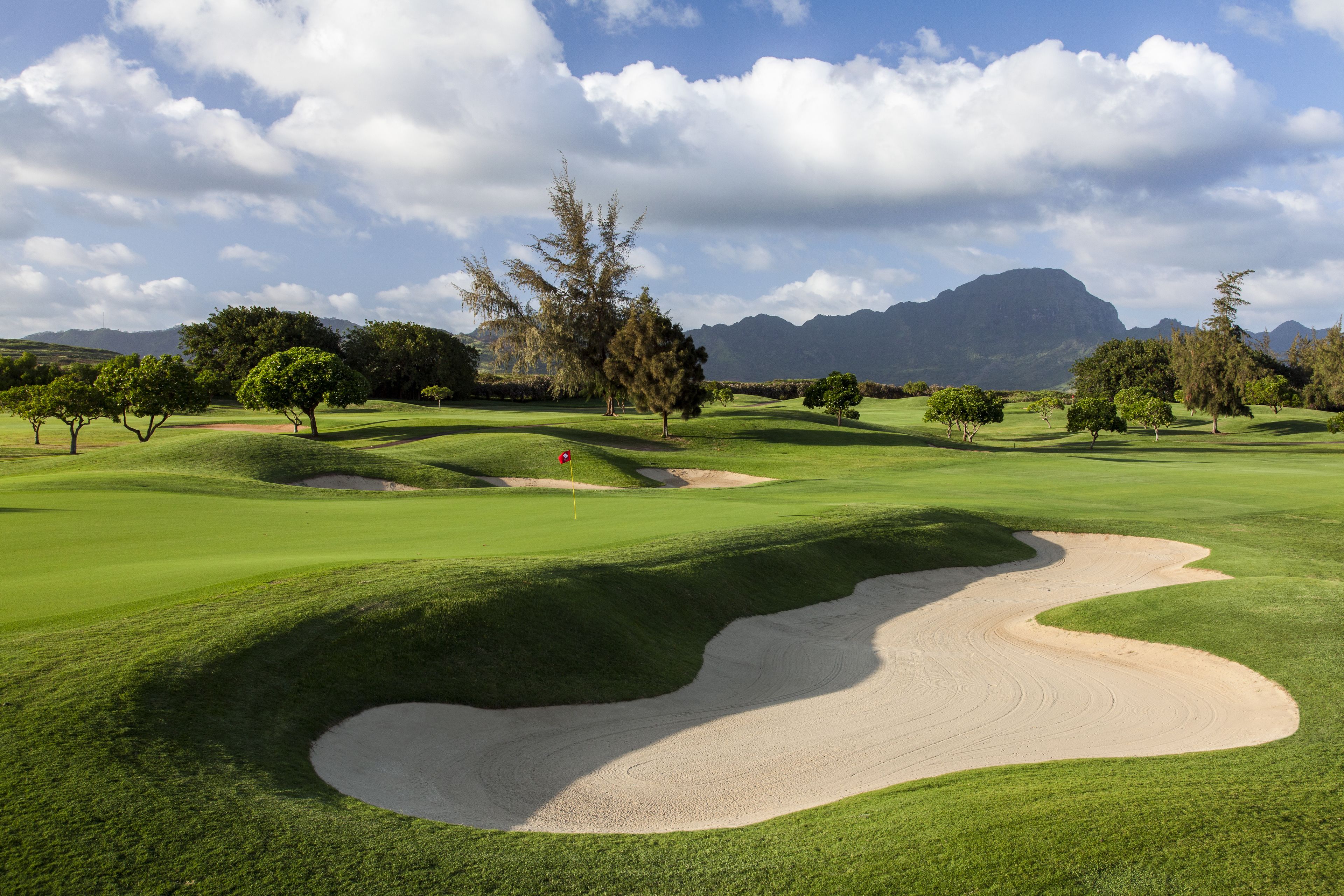 Um campo de golfe com bunkers de areia, árvores e uma montanha ao fundo.