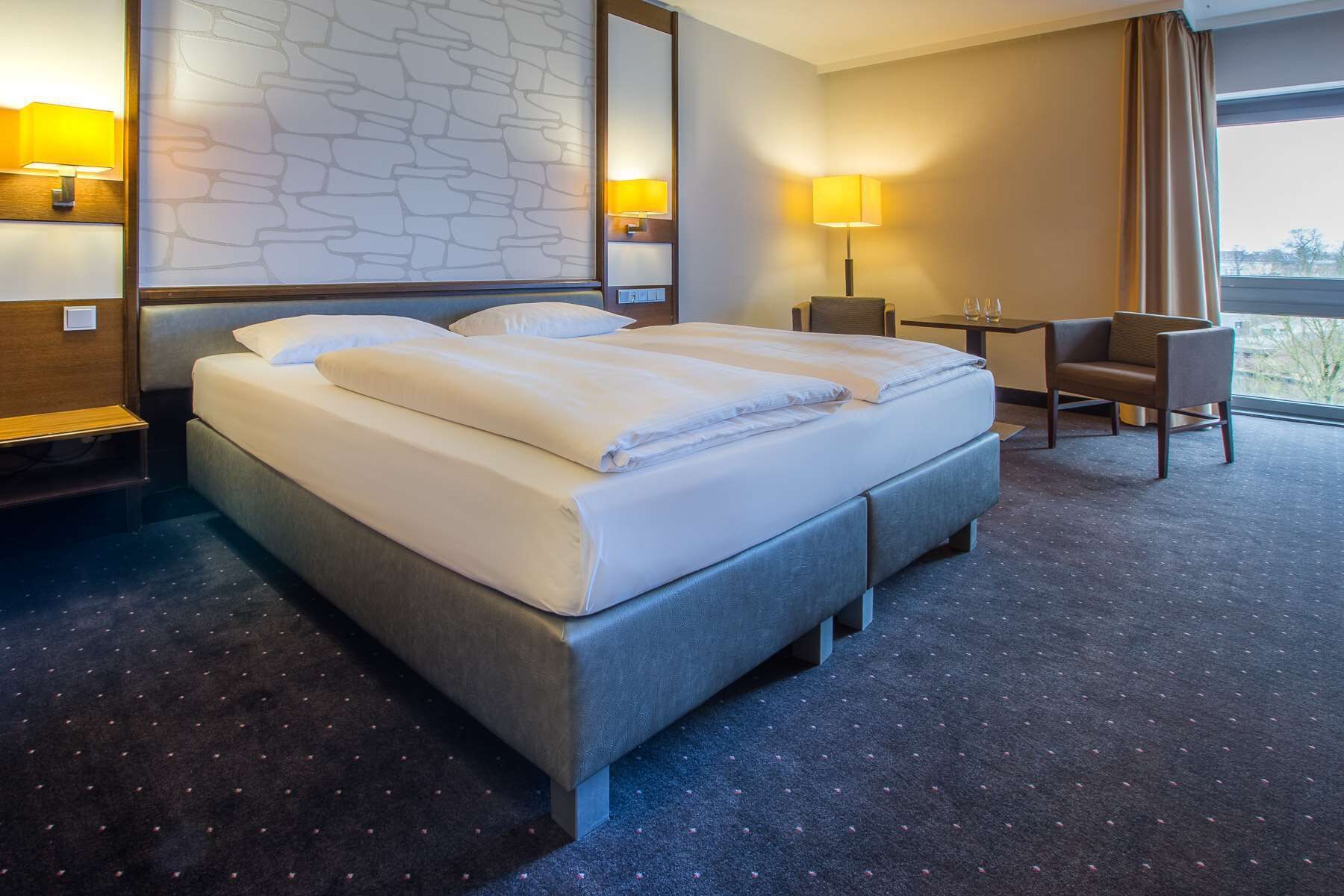 Quarto de hotel com uma cama grande, uma escrivaninha, uma cadeira e vista para o exterior.