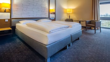 Quarto de hotel com uma cama grande, uma escrivaninha, uma cadeira e vista para o exterior.