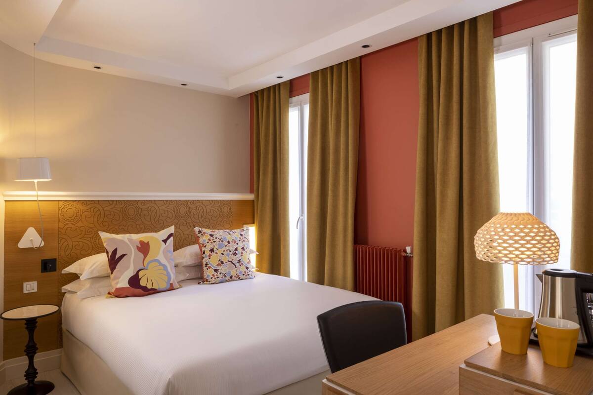 Quarto de hotel com cama, escrivaninha, luminária e cafeteira.