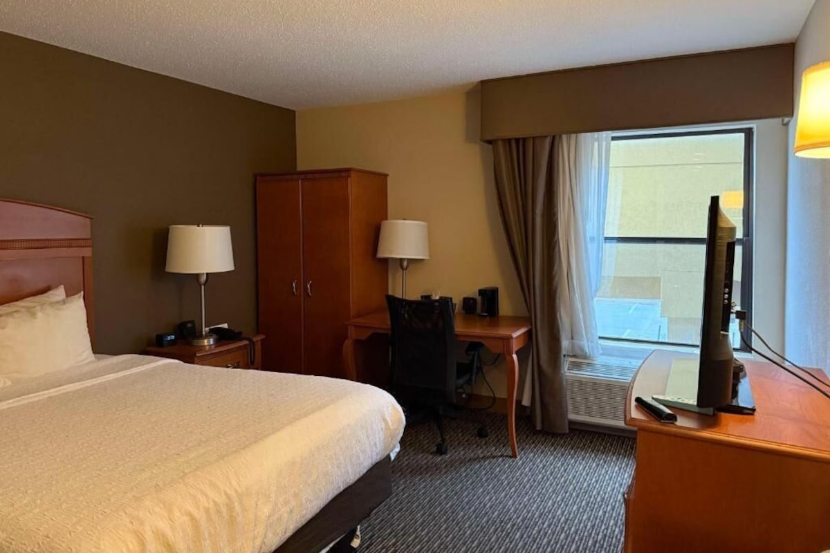 Quarto de hotel com cama, escrivaninha, cadeira e televisão.