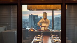 Um chef preparando comida em um restaurante moderno com vista para a cidade.
