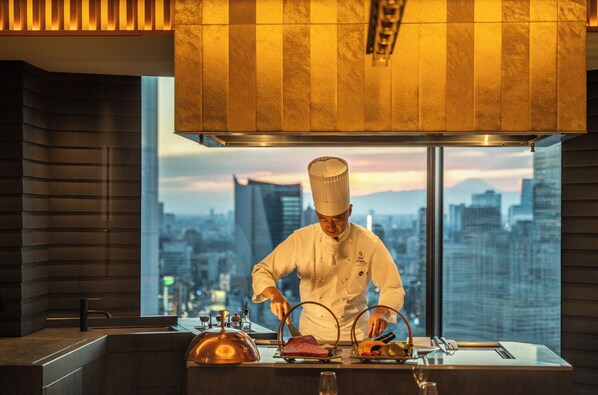Um chef preparando comida em uma cozinha moderna com vista para a cidade.