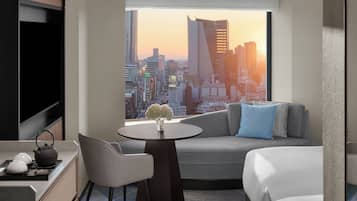 Quarto de hotel moderno com vista para a cidade, um sofá, uma área de refeições e uma televisão.