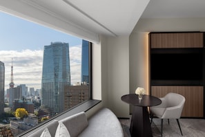 Quarto de hotel moderno com uma grande janela oferecendo vista da cidade, uma mesa redonda com um vaso de flores e uma estante embutida para televisão.