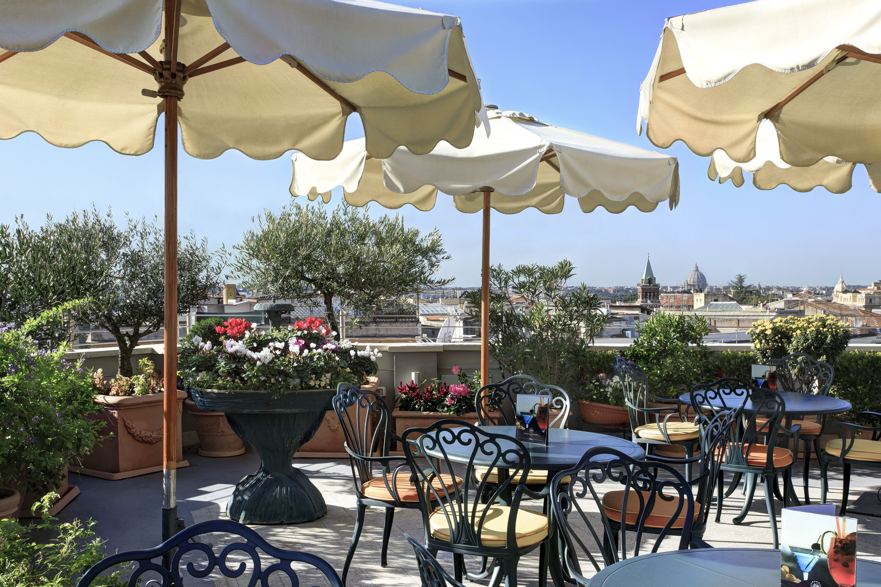 Terraço com mesas ao ar livre, guarda-sóis e plantas em vasos.