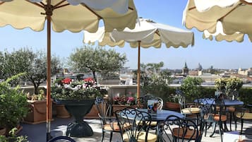 Terraço com mesas ao ar livre, guarda-sóis e plantas em vasos.