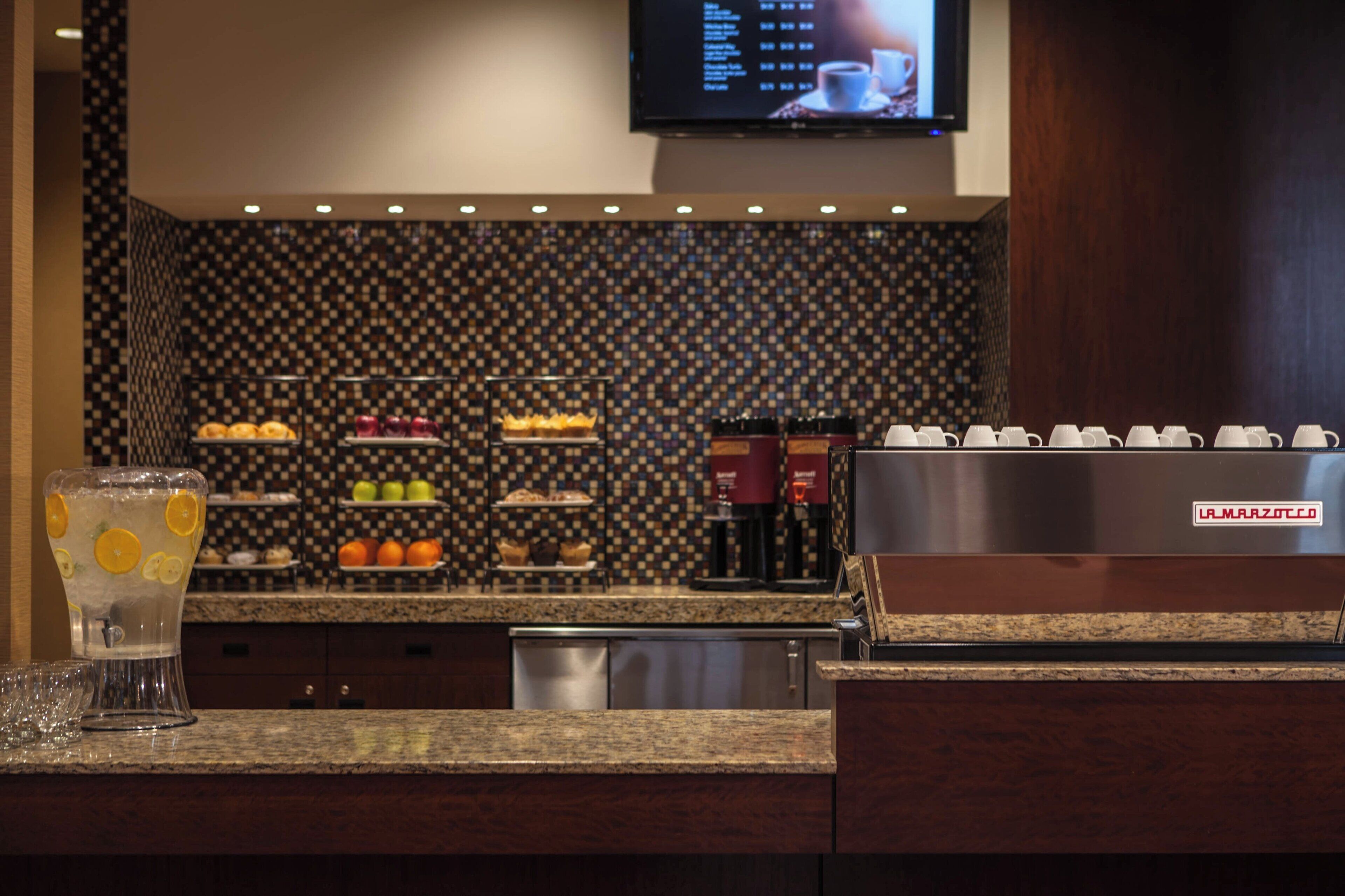 Uma cozinha de hotel com máquina de café, dispensador de bebidas e tela de menu.