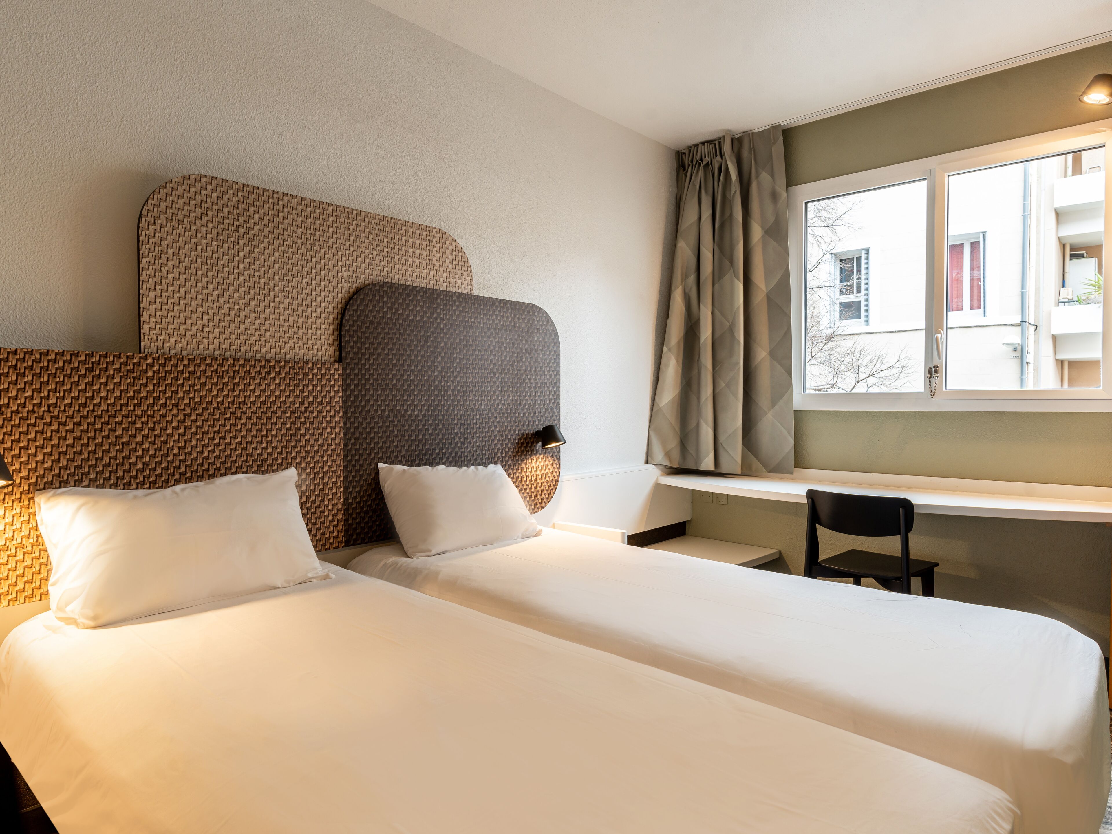 Quarto de hotel com duas camas, uma mesa e uma cadeira.