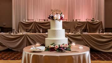 Bolo de casamento em vários andares, com a inscrição 'Mr & Mrs' no topo, sobre uma mesa redonda com toalha, rodeado por velas e arranjos florais.