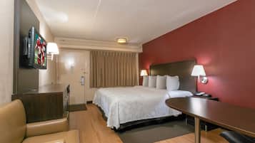 Quarto de hotel com cama, mesas de cabeceira, escrivaninha, cadeira e televisão.