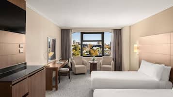 Quarto de hotel com cama, escrivaninha, cadeira e televisão.