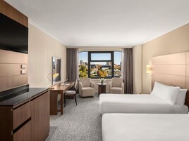 Quarto de hotel com cama, escrivaninha, cadeira e televisão.