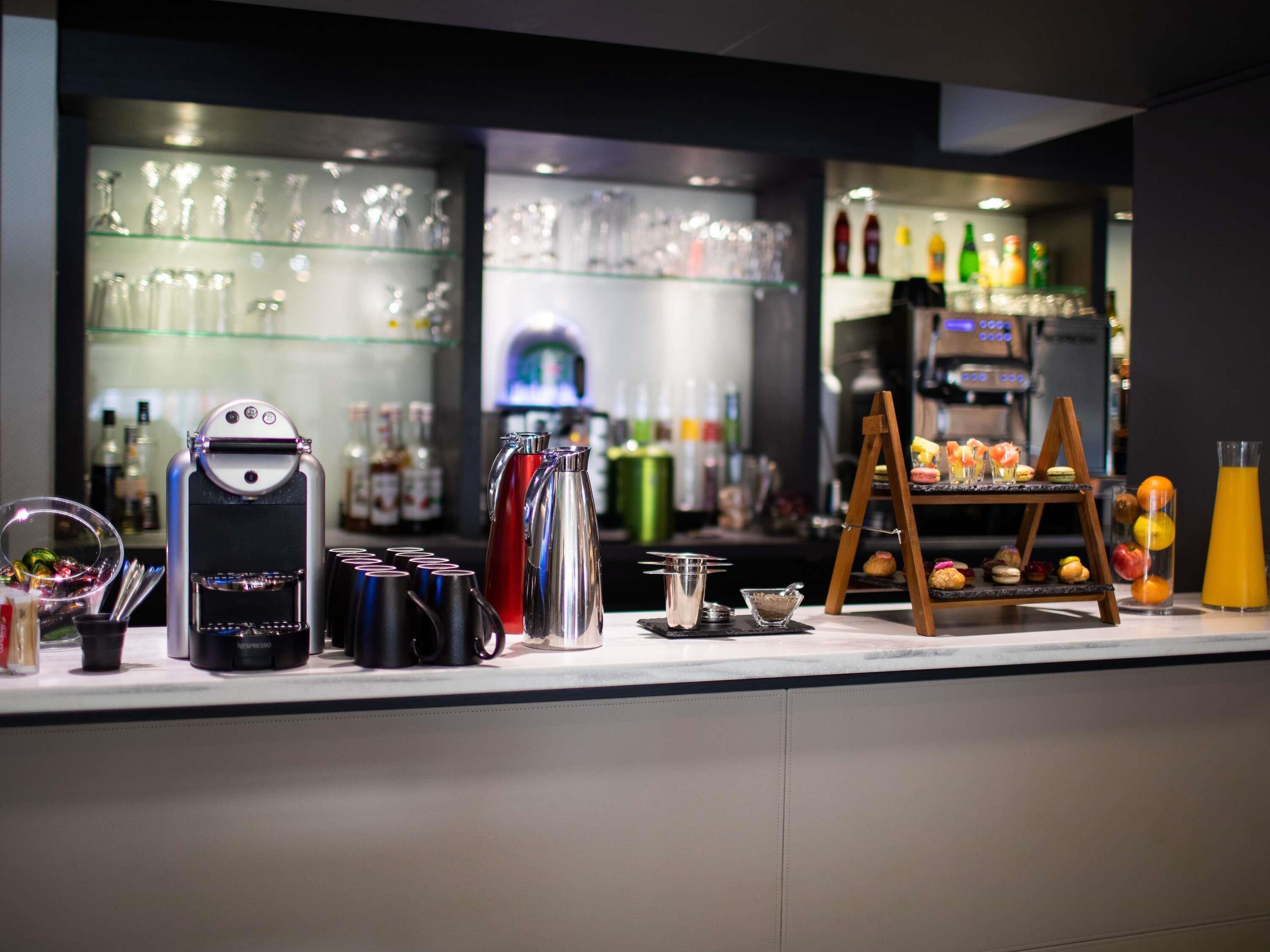 Uma área de bar com máquina de café, diversos dispensadores de bebidas, petiscos expostos e seleção de bebidas engarrafadas.