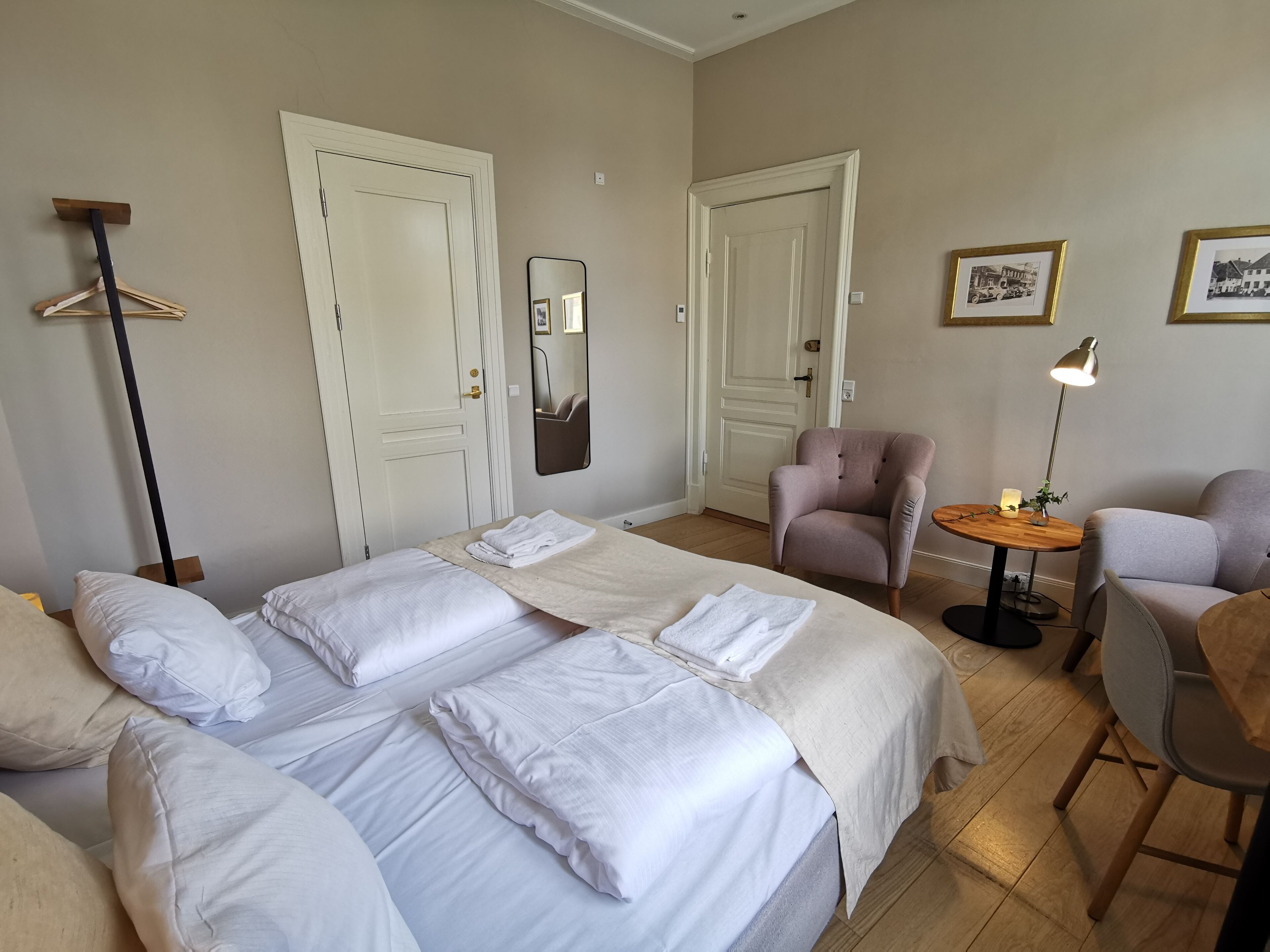 Quarto de hotel com uma cama grande, uma cadeira, uma mesinha de cabeceira com abajur e um espelho na parede.