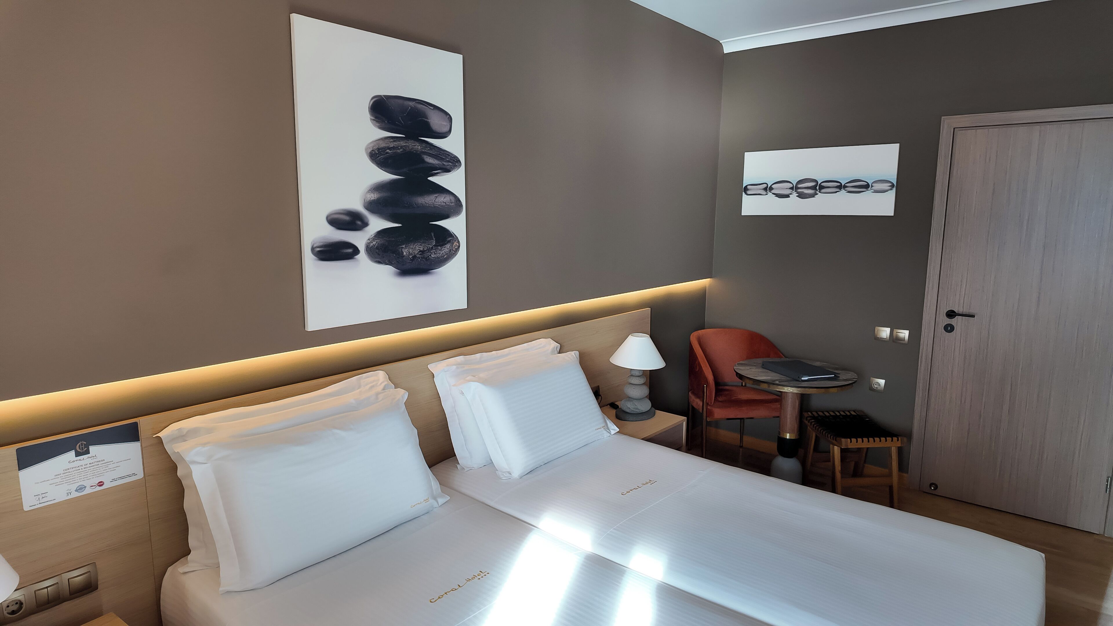 Quarto de hotel com cama, mesa de cabeceira, poltrona, mesinha e obras de arte nas paredes.