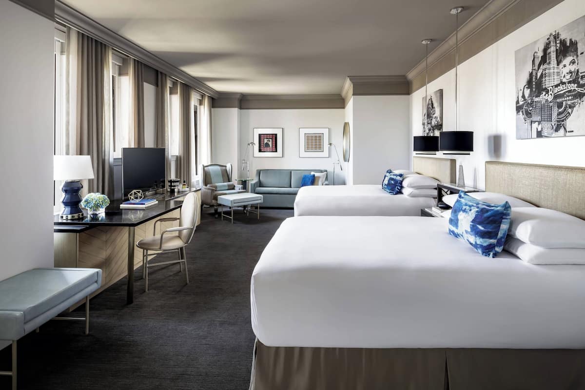Quarto de hotel com uma cama grande, uma escrivaninha com computador, um sofá e uma televisão.
