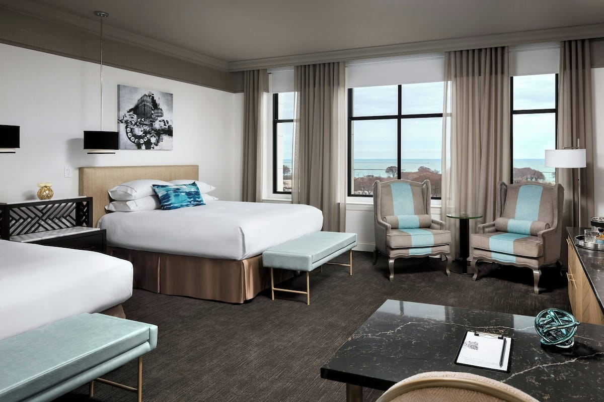 Quarto de hotel com uma cama grande, duas poltronas, uma mesinha e vista para o mar.
