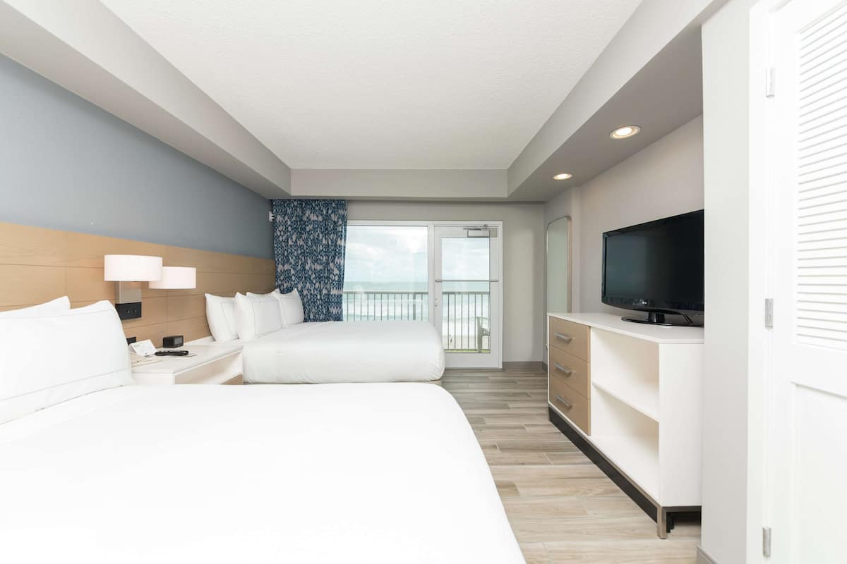 Quarto de hotel com cama grande, televisão, escrivaninha e varanda com vista.