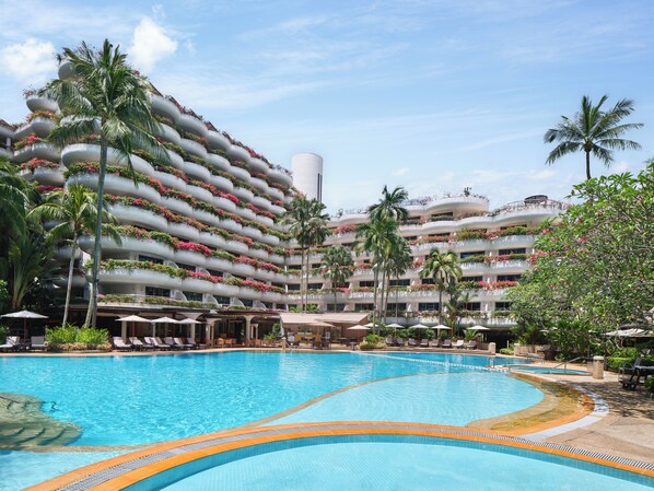 Um hotel com várias varandas decoradas com flores, piscina e palmeiras.