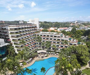Um hotel com várias andares, varandas, piscina e vegetação exuberante.