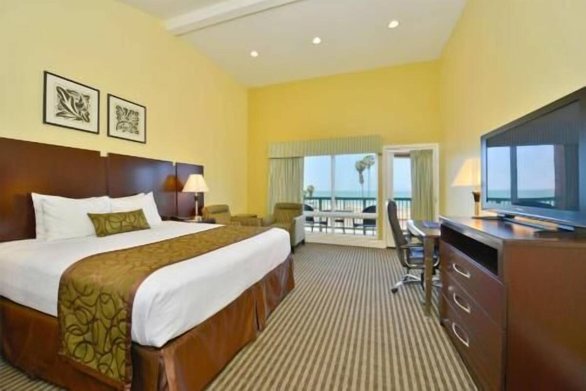 Quarto de hotel com cama grande, televisão, escrivaninha e varanda com vista.
