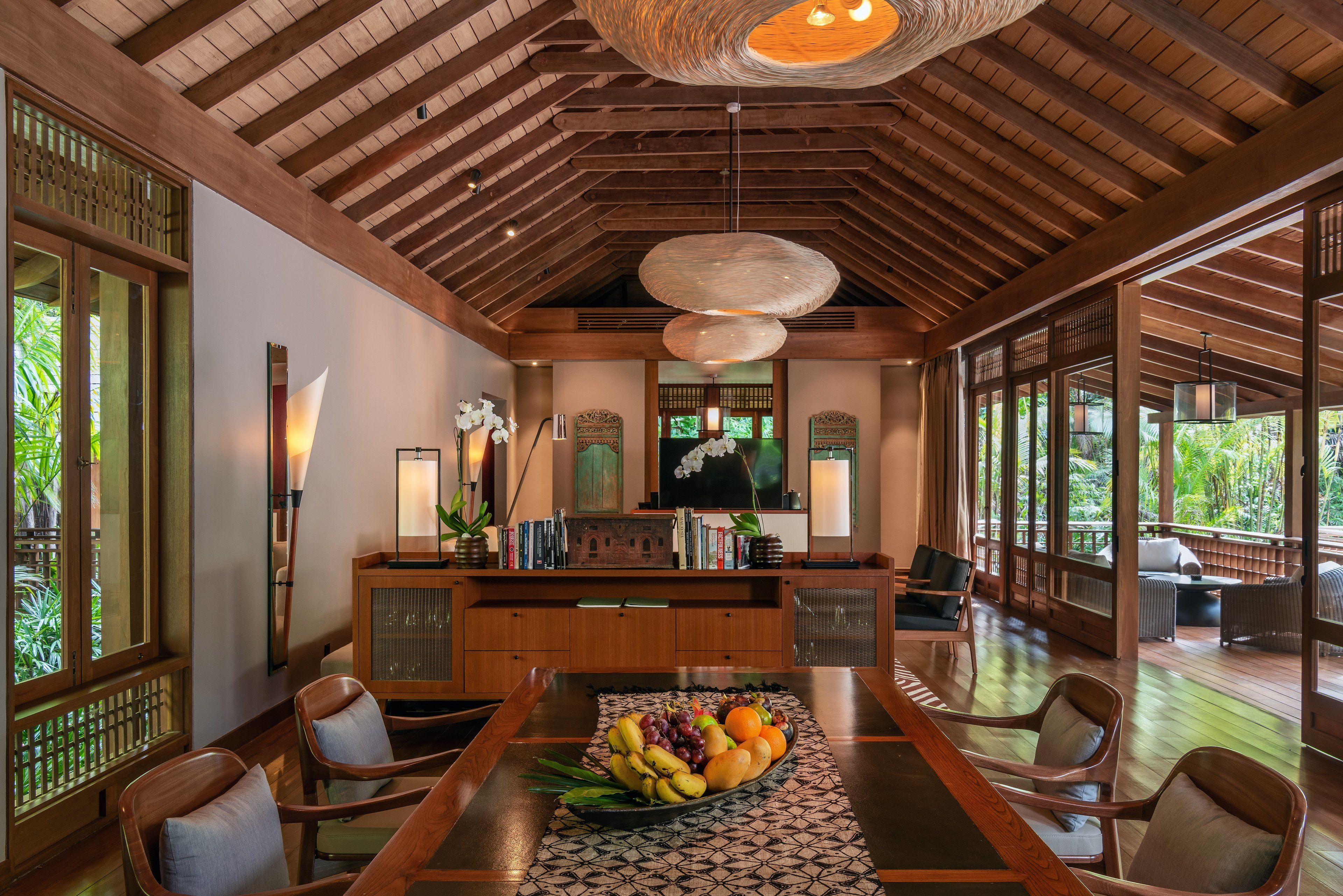 Um quarto espaçoso com teto de madeira, uma mesa de jantar com arranjo de frutas e uma área de estar com cadeiras.