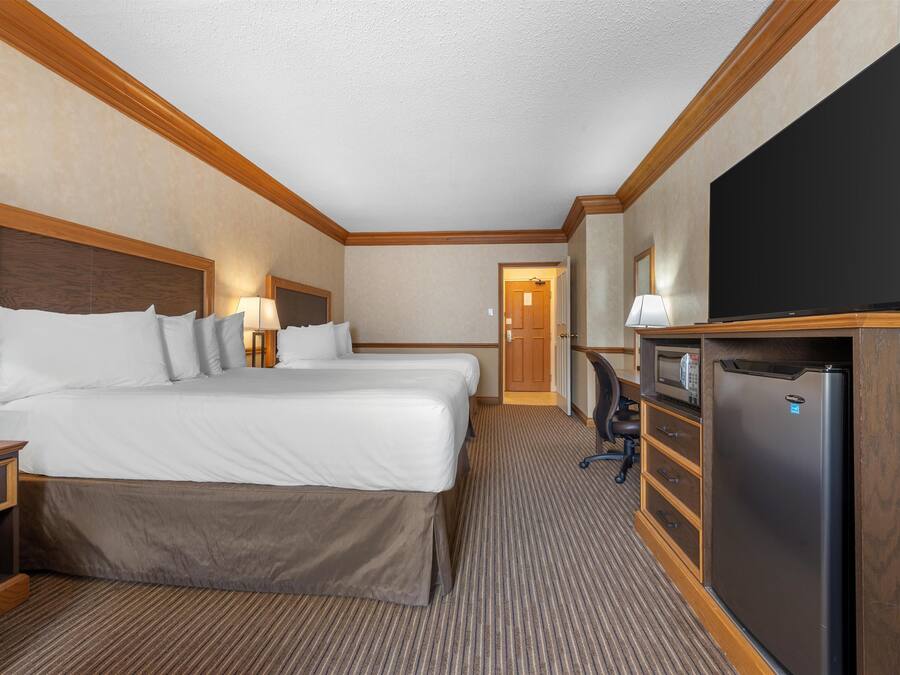 Quarto de hotel com duas camas, televisão, frigorífico e secretária com candeeiro.