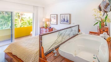 Quarto com cama grande, banheira, varanda com paredes amarelas e vista para o verde.