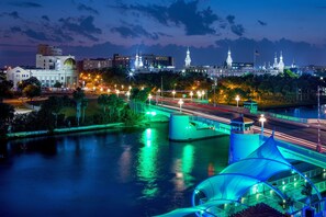 Paisagem urbana noturna com rio, edifícios iluminados e uma ponte.
