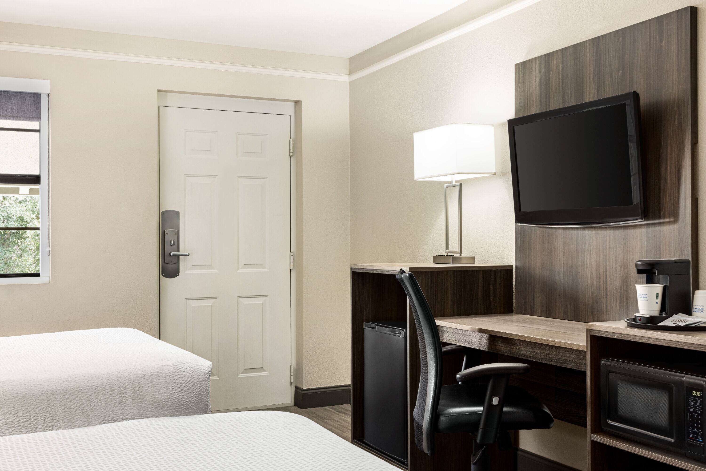 Quarto de hotel com duas camas, uma escrivaninha com cadeira, televisão, cafeteira e micro-ondas.