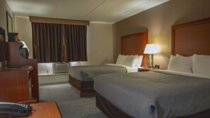Quarto de hotel com duas camas, uma escrivaninha, telefone e janela com cortinas.