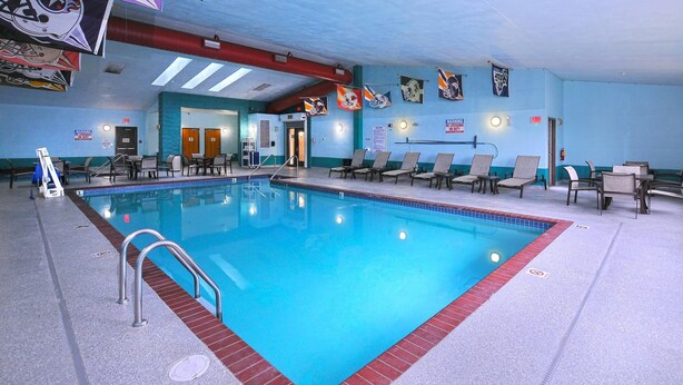 Piscina interna com espreguiçadeiras, posto de salva-vidas e detalhes decorativos nas paredes.