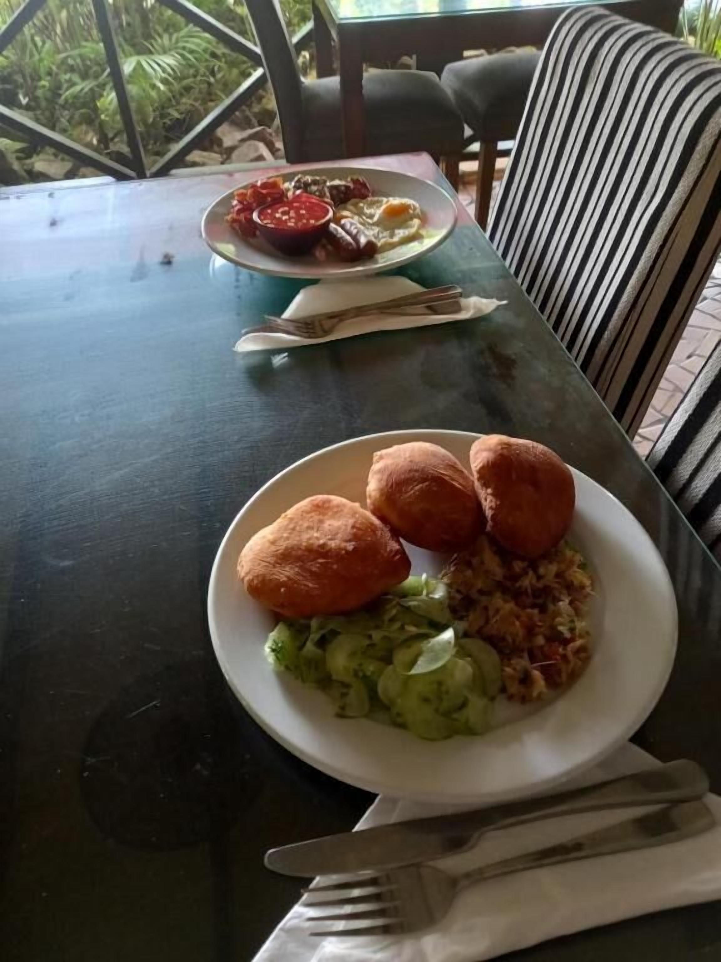 Uma mesa com um prato de comida, incluindo duas porções redondas e uma salada, além de um garfo e uma faca sobre um guardanapo.