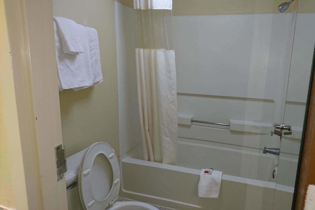 Casa de banho com sanita, chuveiro com porta de vidro e toalha pendurada na parede.