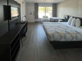 Quarto de hotel moderno com uma cama grande, televisão de tela plana na parede, escrivaninha com cadeira e janela com cortinas.