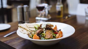 Uma salada em uma tigela com vários legumes e um pedaço de carne sobre uma mesa de madeira.