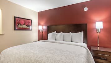 Quarto de hotel com uma cama grande, mesa de cabeceira, abajur e quadro na parede.