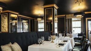 Um restaurante com assentos estofados em preto, toalhas de mesa brancas e detalhes dourados.