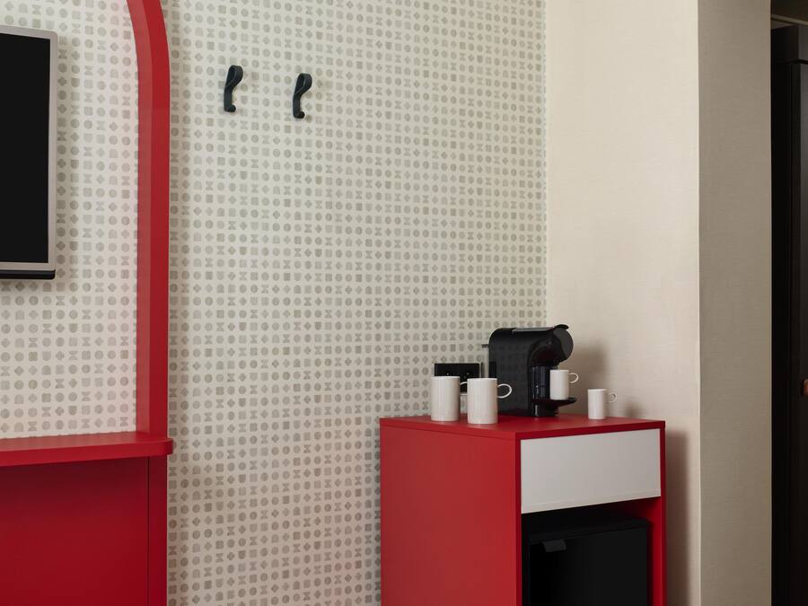 Quarto de hotel com esquema de cores vermelho e branco, uma cafeteira e duas chávenas sobre uma mesa pequena.