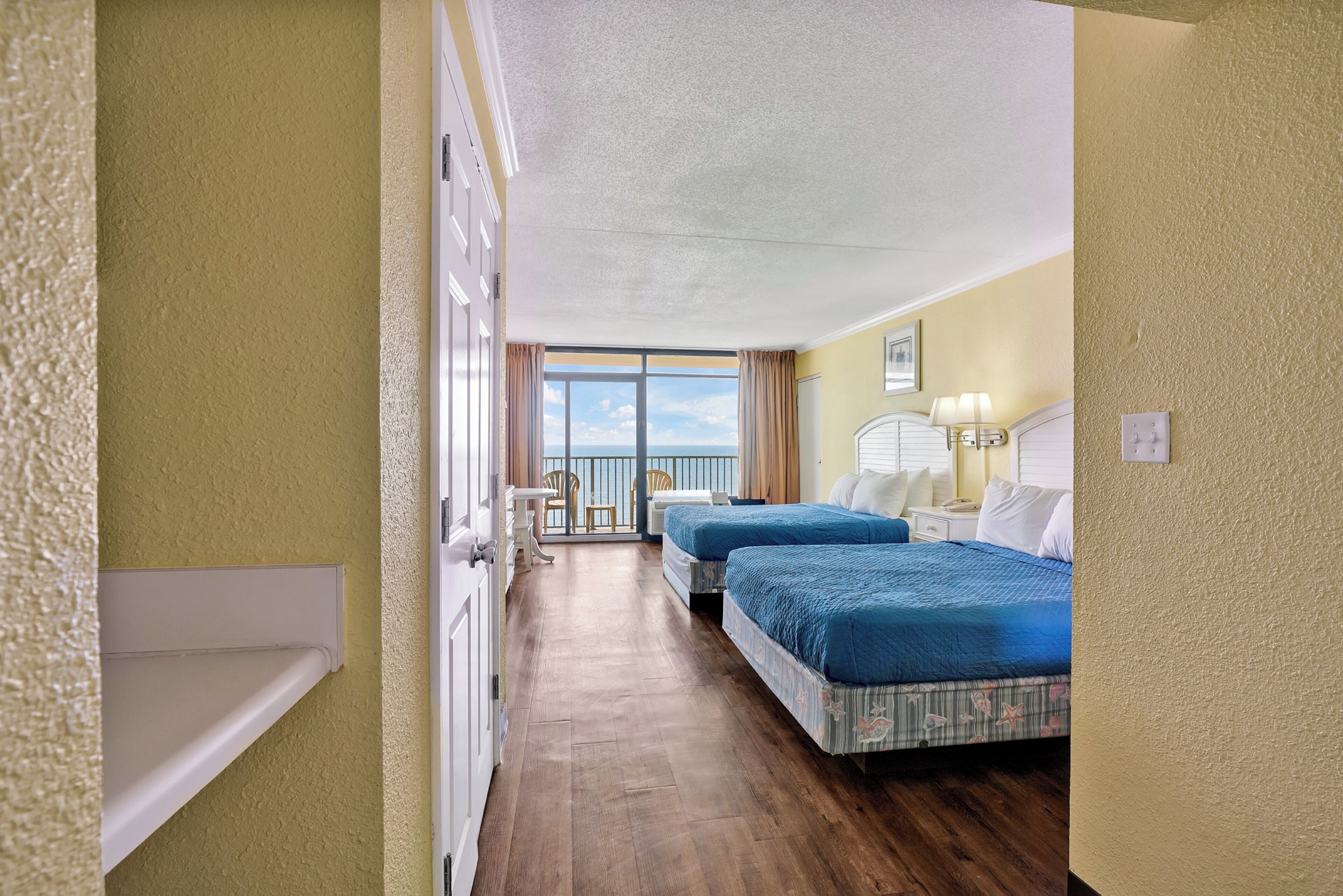 Quarto de hotel com duas camas, varanda, uma pequena mesa com cadeiras e vista do céu.