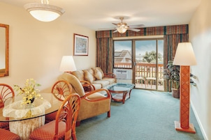 Quarto de hotel com varanda, área de jantar com mesa e cadeiras, sofá e ventilador de teto.