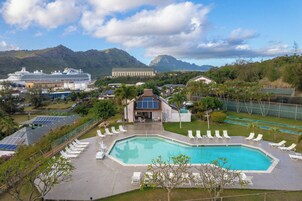 Piscina com espreguiçadeiras, um edifício com painéis solares e um cruzeiro ao fundo.